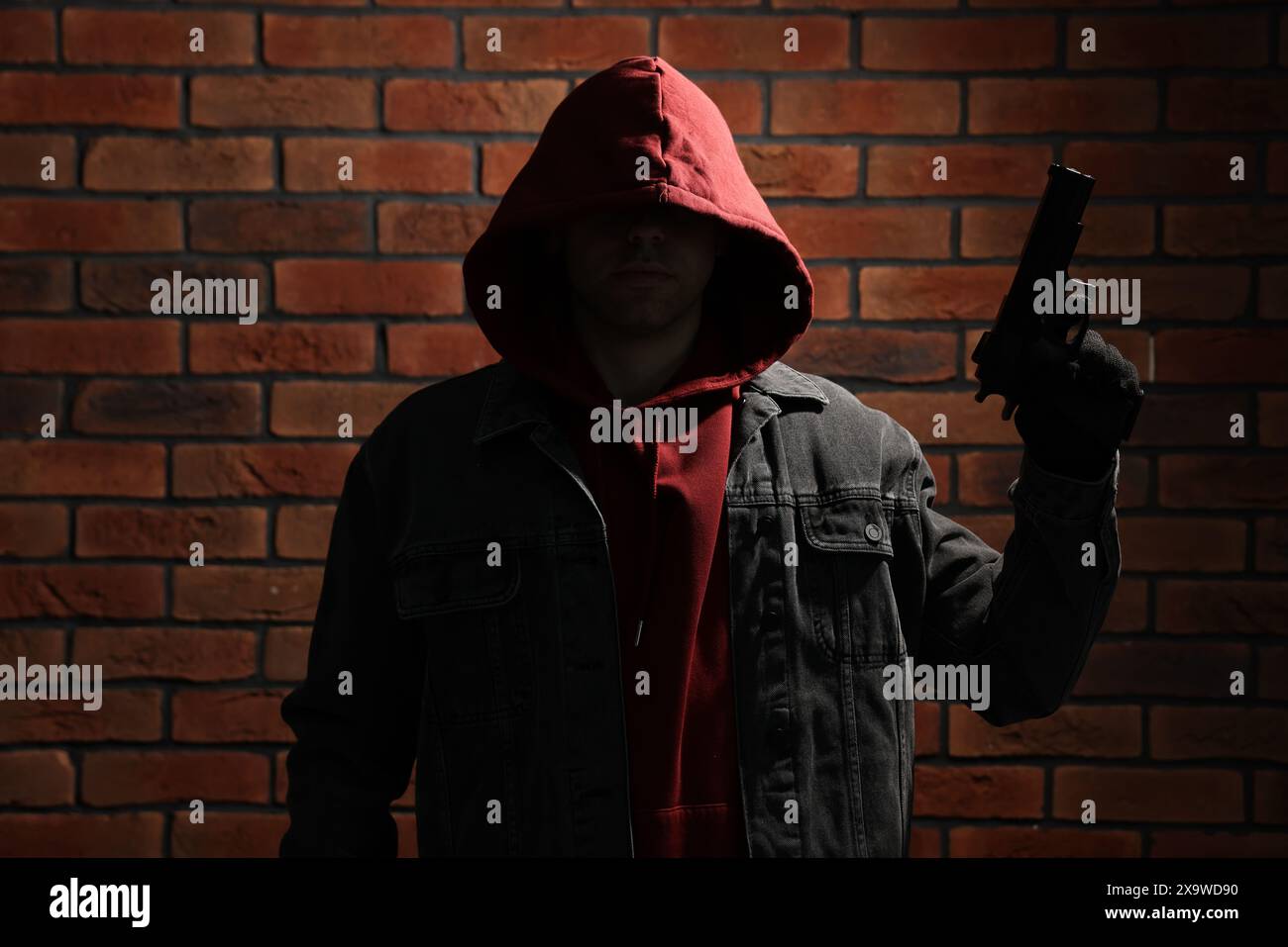 Thief in hoodie with gun against red brick wall Stock Photo - Alamy