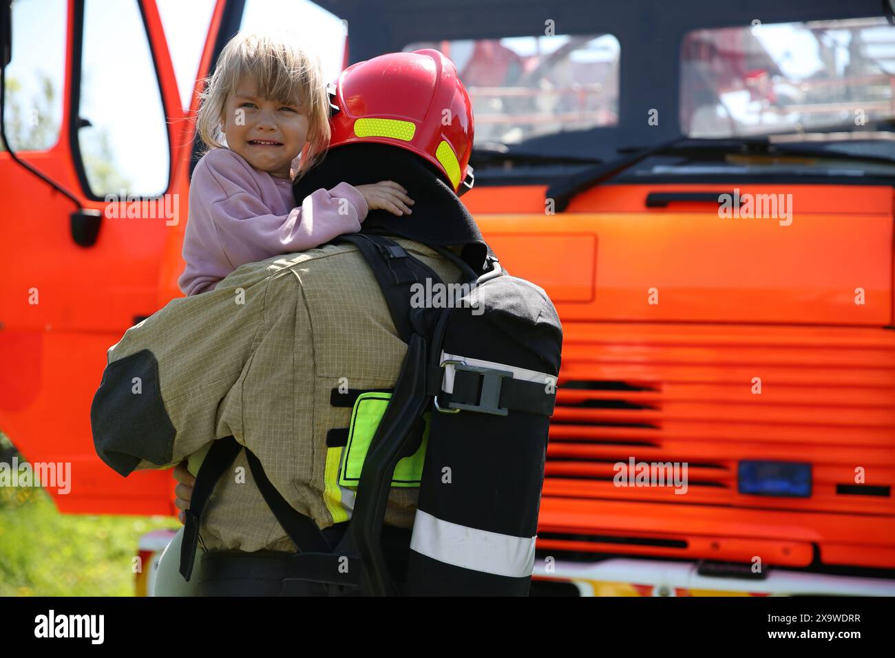 Firefighter in uniform holding rescued little girl near fire truck ...