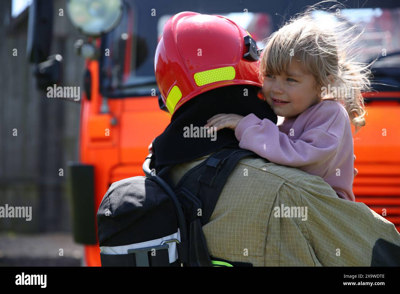 Firefighter in uniform holding rescued little girl near fire truck ...