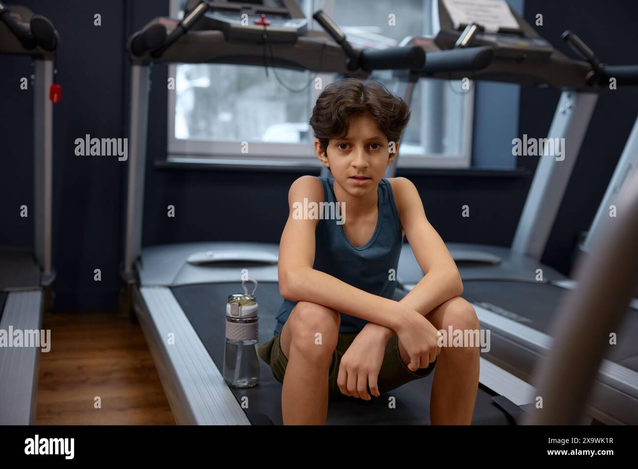 Portrait of fatigue preteen boy having rest after training on treadmill ...