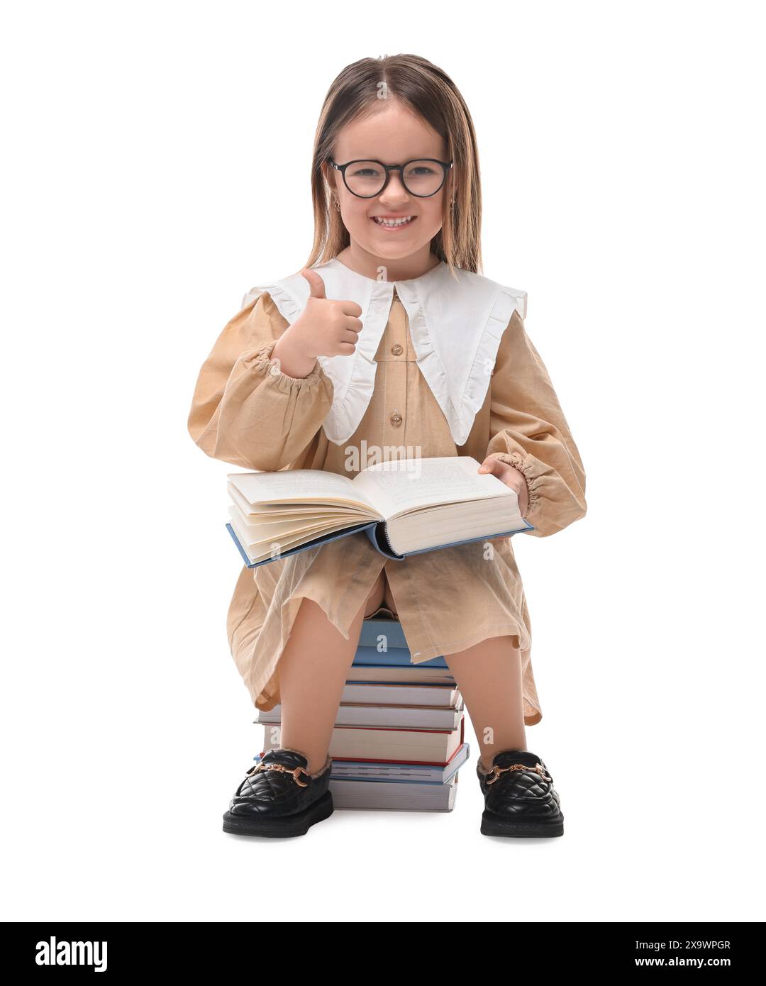 Cute little girl with books showing thumbs up against white background ...