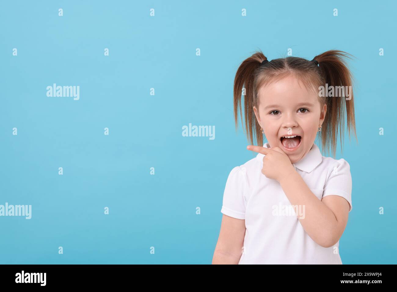 Portrait of emotional little girl pointing at something on light blue ...