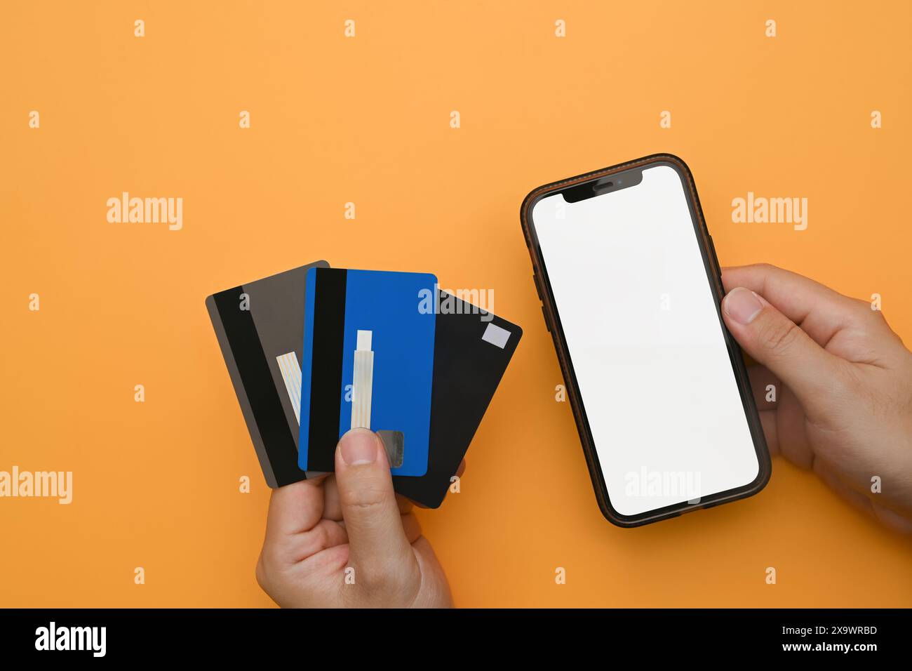 Hand holding mobile phone and bank cards over yellow background. Modern ...