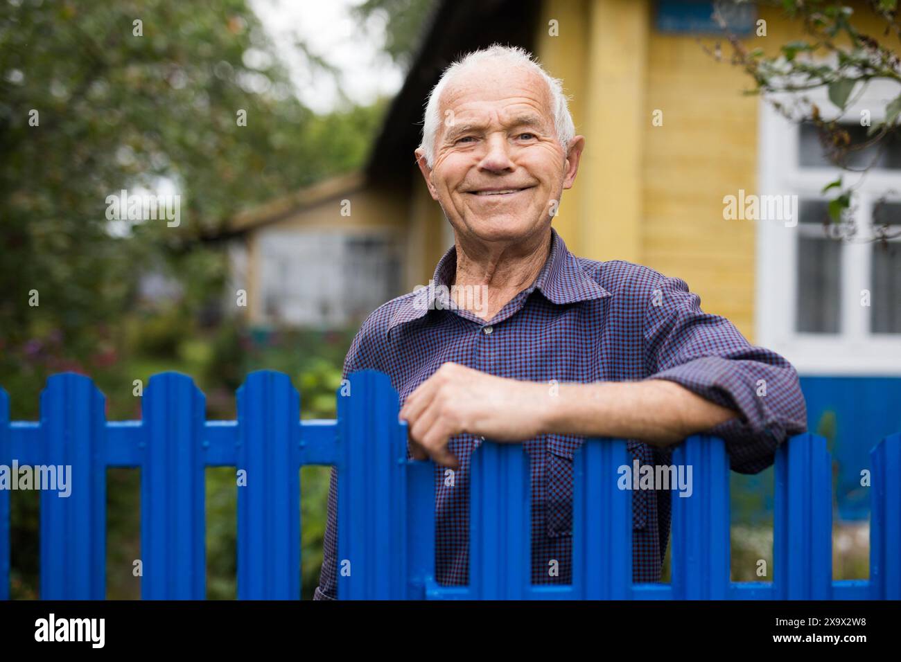 Portrait of gray-haired owner at fence of his country house in village ...