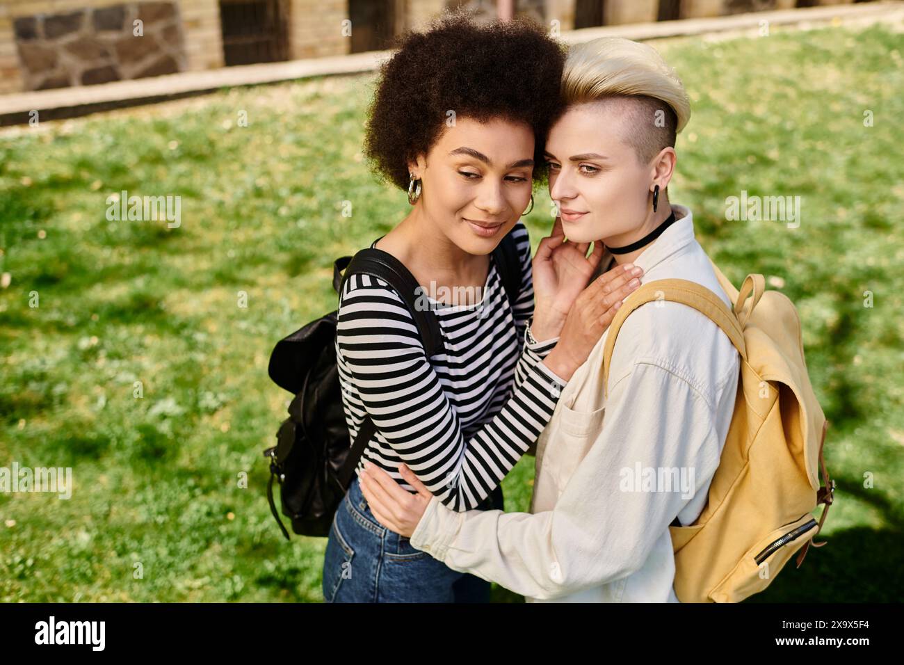 Two young women, in casual attire, embrace lovingly in the grassy field ...