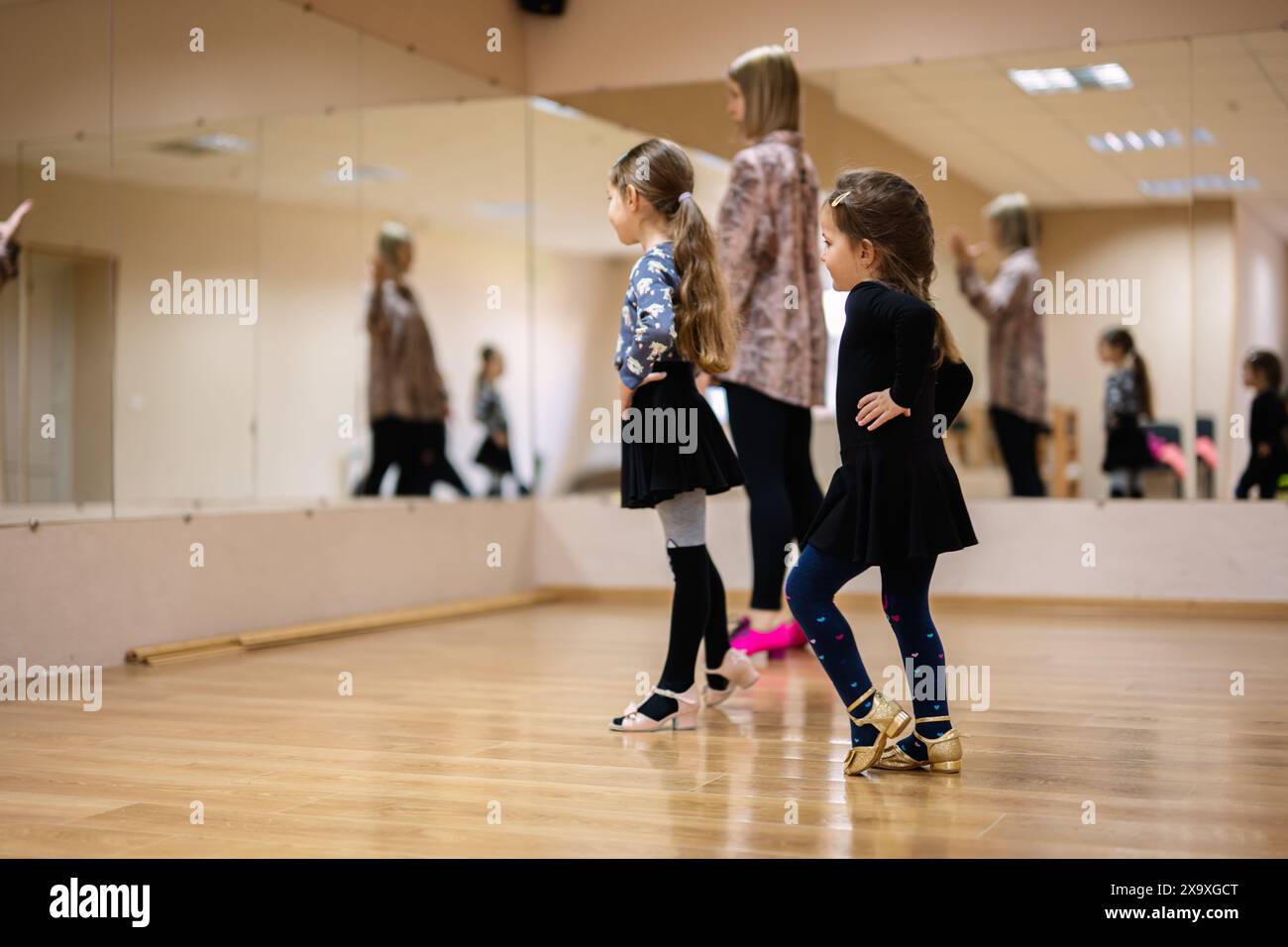 Young girls learning ballet poses with their instructor guiding them in ...