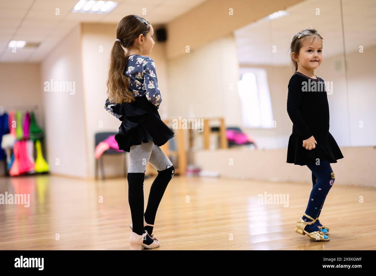 Two young girls practicing dance routines in a studio with a wooden ...