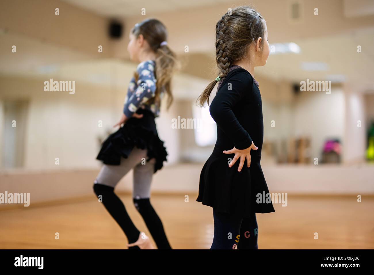 Two young girls practicing dance in a classroom with mirrors and a ...