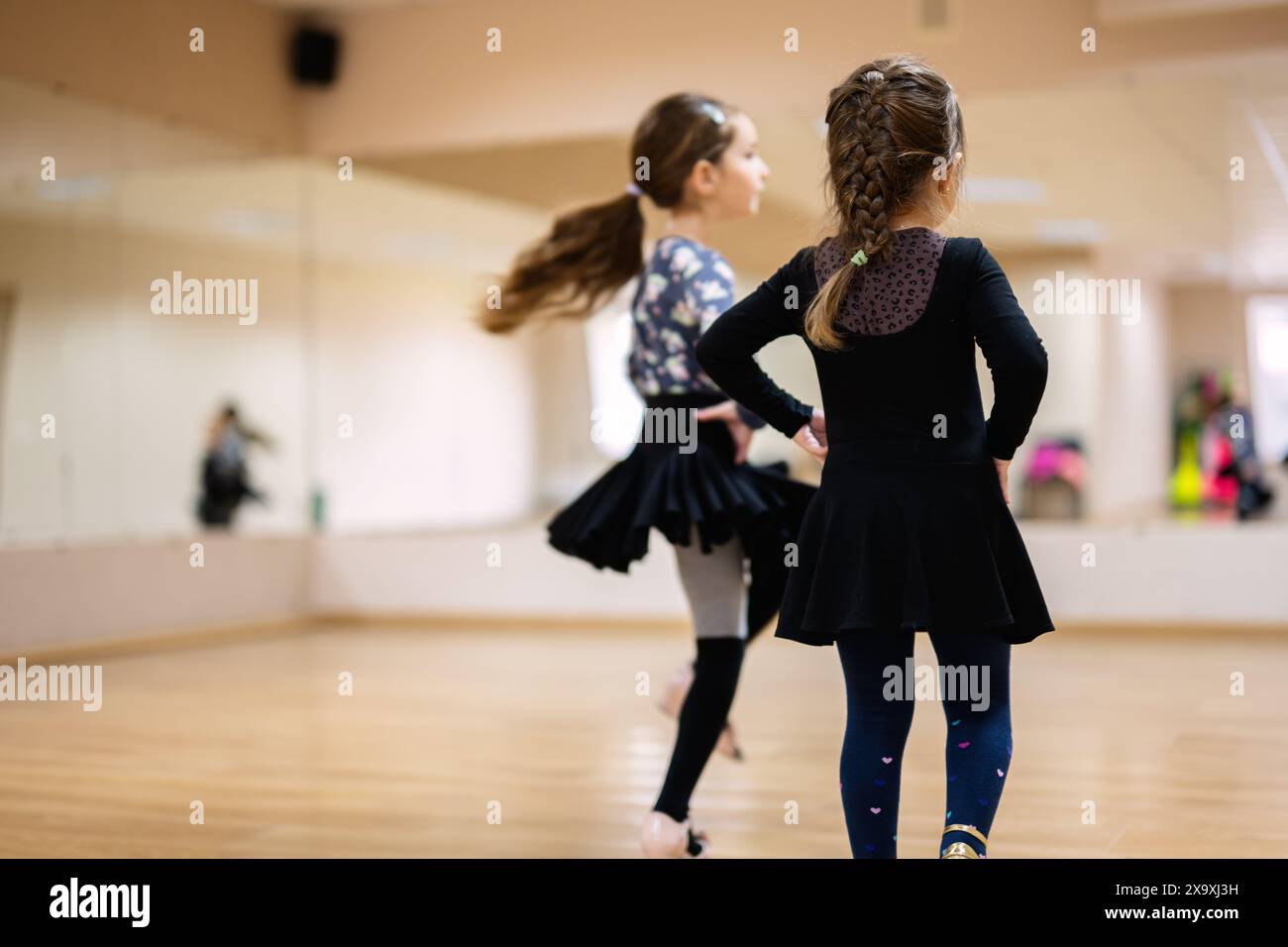 Two young girls dance together in a ballet studio with wooden floors and mirrors, showcasing joy ...