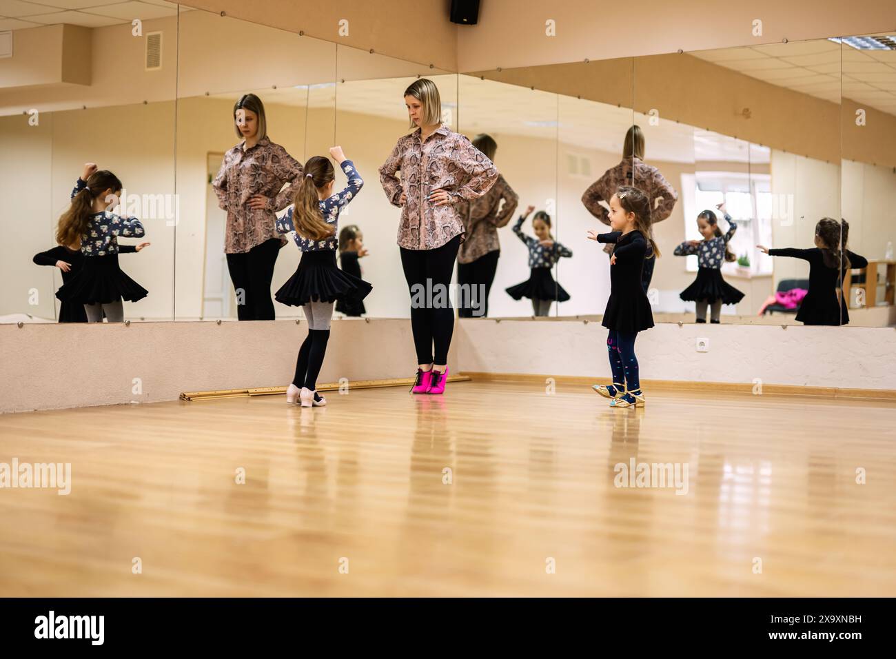 A dance instructor guiding young girls in a ballet studio with mirrored ...