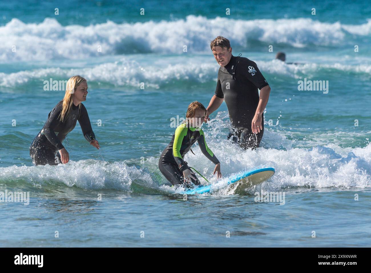 A mother and father helping their young daughter learning to surf at ...