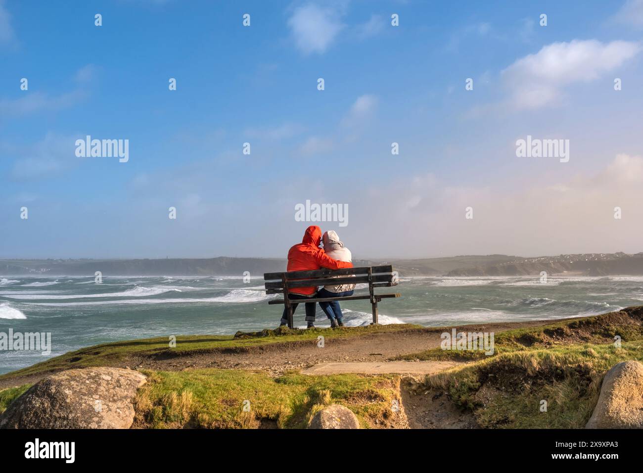 A couple sitting on a bench with their hoods up in high wind brought by ...