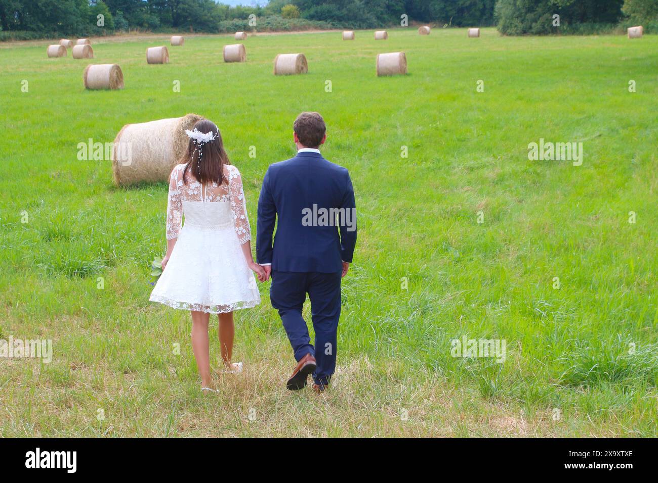 Bride and groom walking towards a green field with hay bales on wedding ...