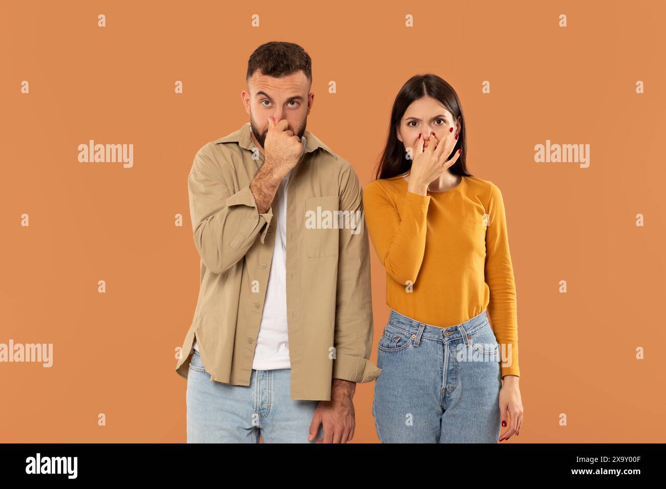 Two People Posing Silly With Hand Over Nose Against Orange Stock Photo ...