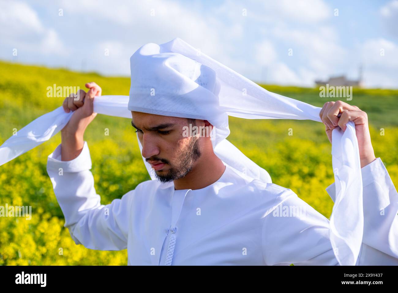 A man in a white dishdasha and kandura stands in a field of yellow ...
