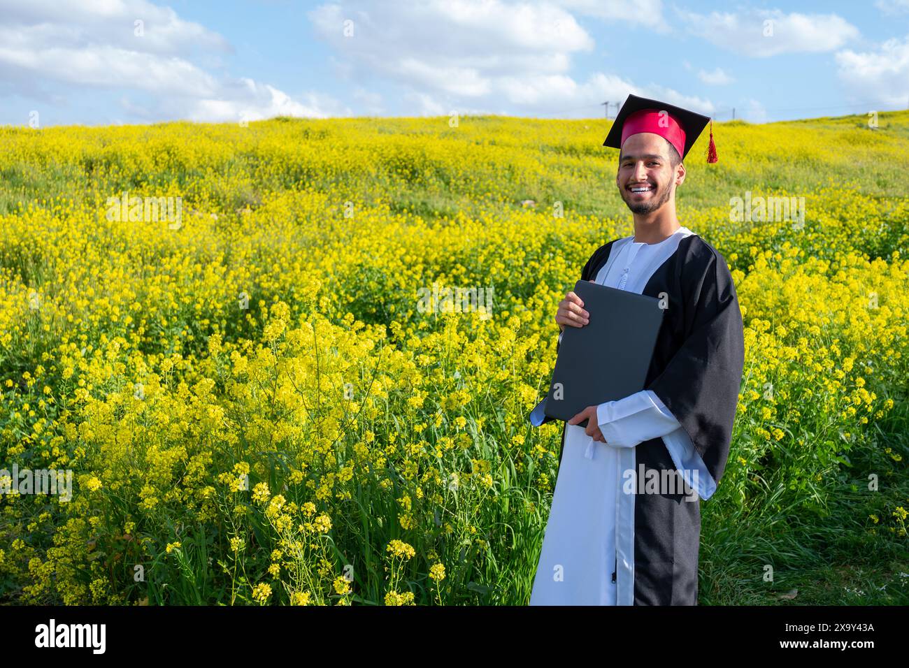 A joyful young Middle-Eastern man in a graduation cap and gown stands ...