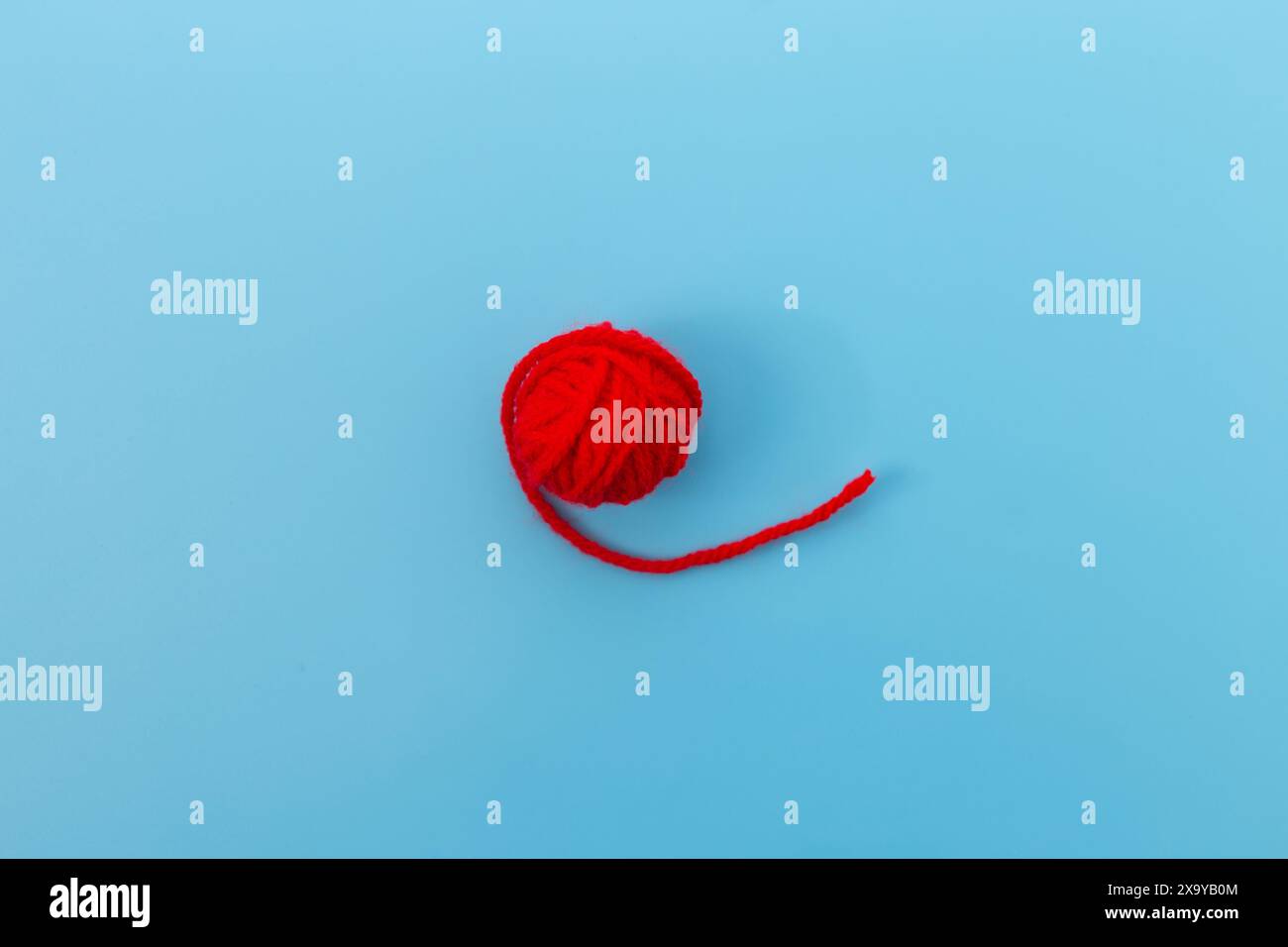 a small red ball of yarn lying on a plain blue background. This image ...