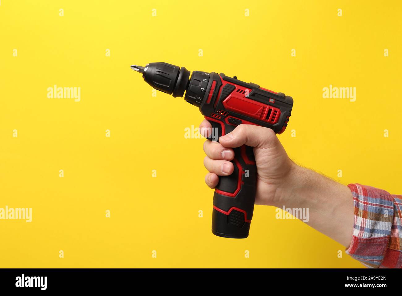 Handyman holding electric screwdriver on yellow background, closeup ...