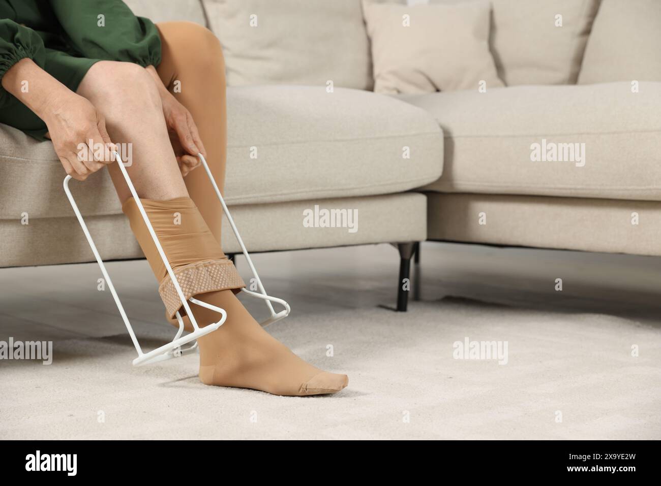 Woman putting on compression garment with stocking donner in living ...