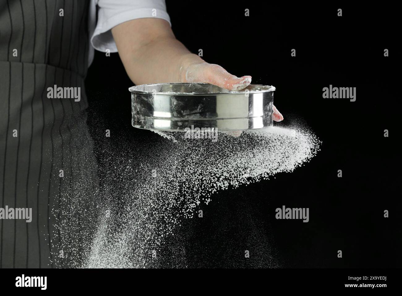 Woman sieving flour at table against black background, closeup Stock ...