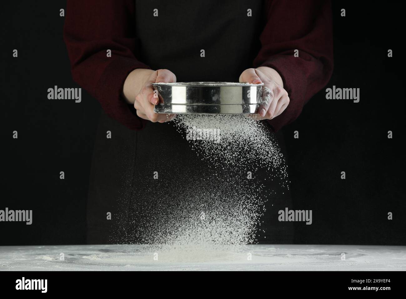 Woman sieving flour at table against black background, closeup Stock ...