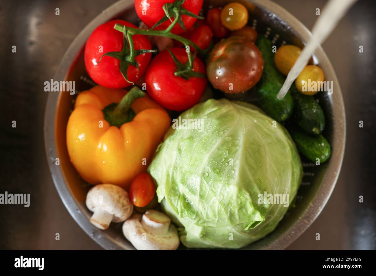 Washing different vegetables with tap water in metal colander inside ...