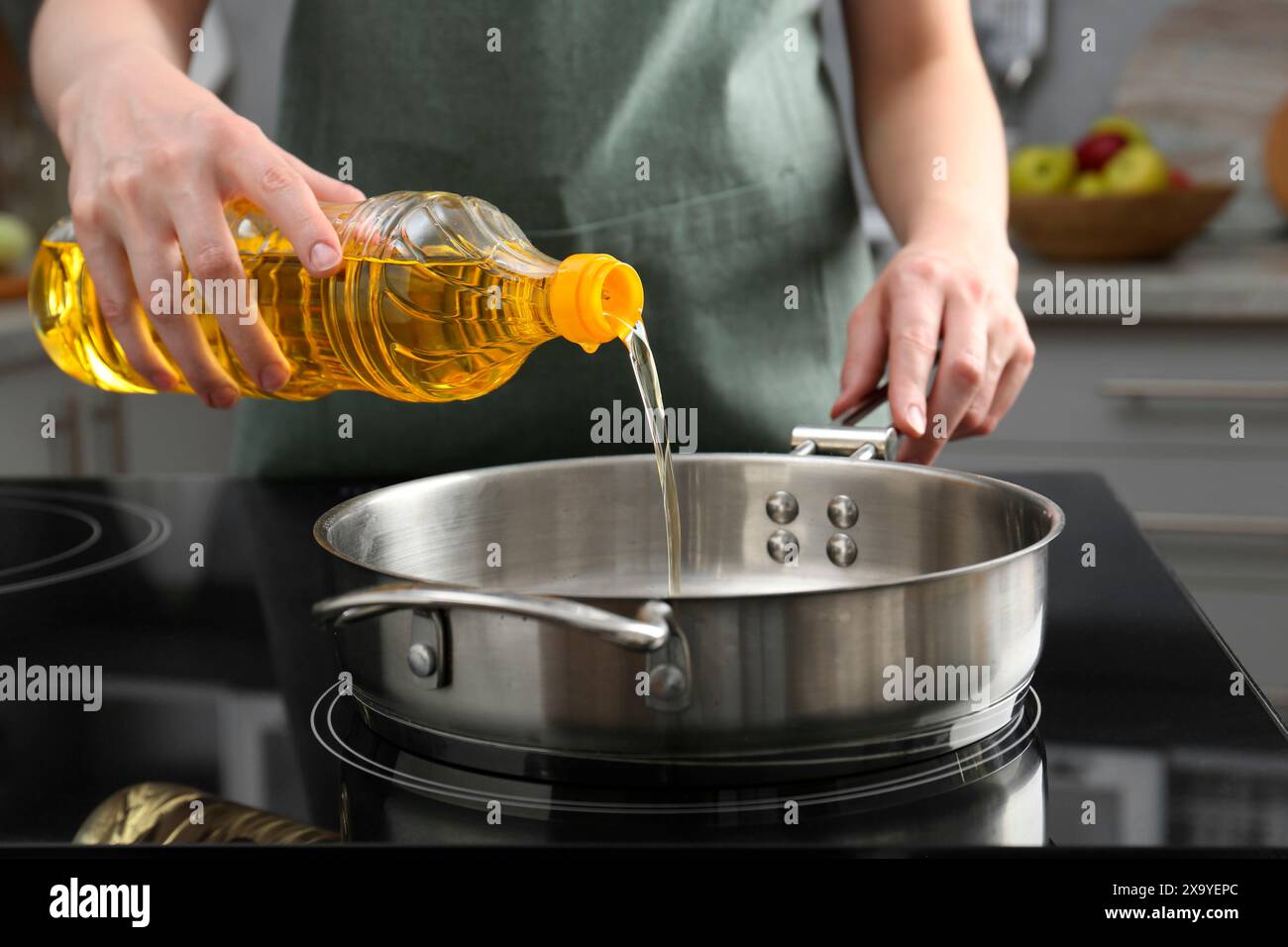 Vegetable fats. Woman pouring oil into frying pan on stove in kitchen ...