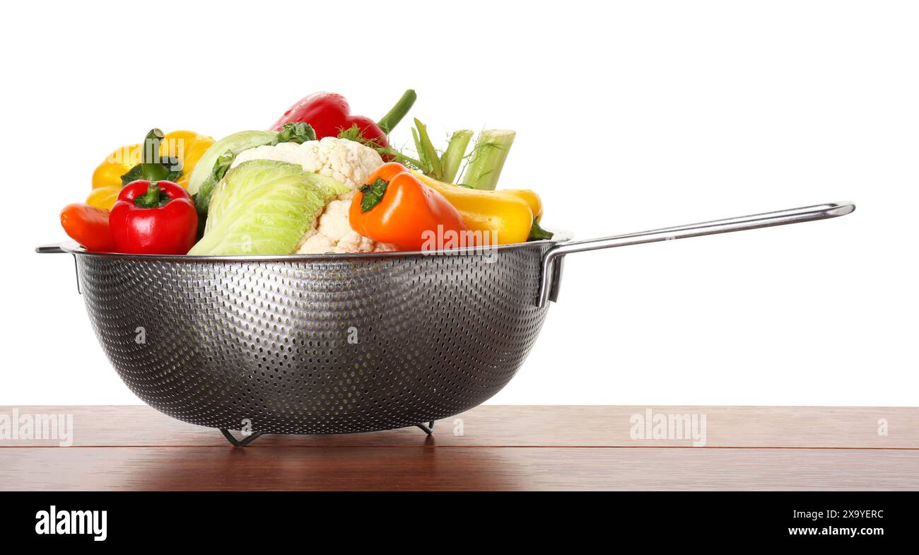 Metal colander with different vegetables on wooden table against white ...
