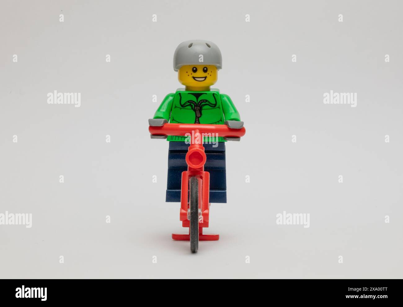 A Lego minifigure of a boy with a safety helmet riding a red bicycle ...
