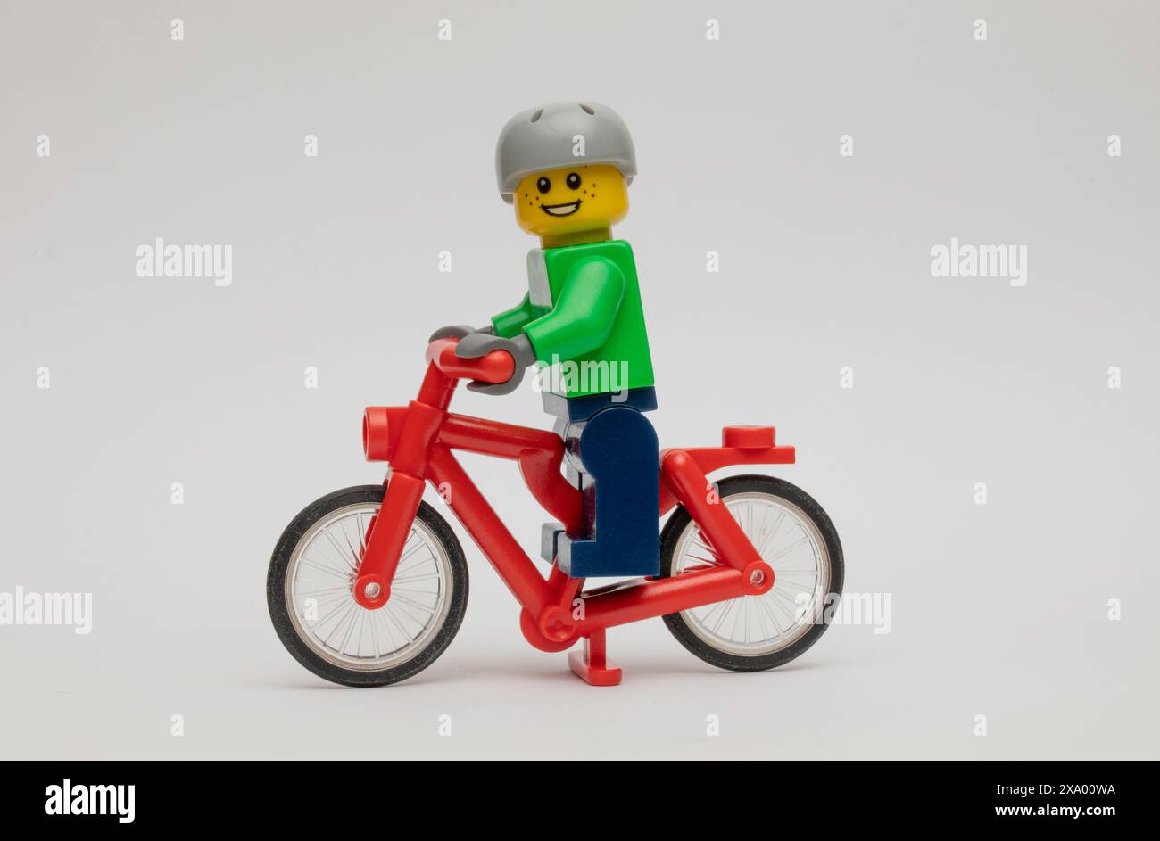 A Lego minifigure of a boy with a safety helmet riding a red bicycle ...