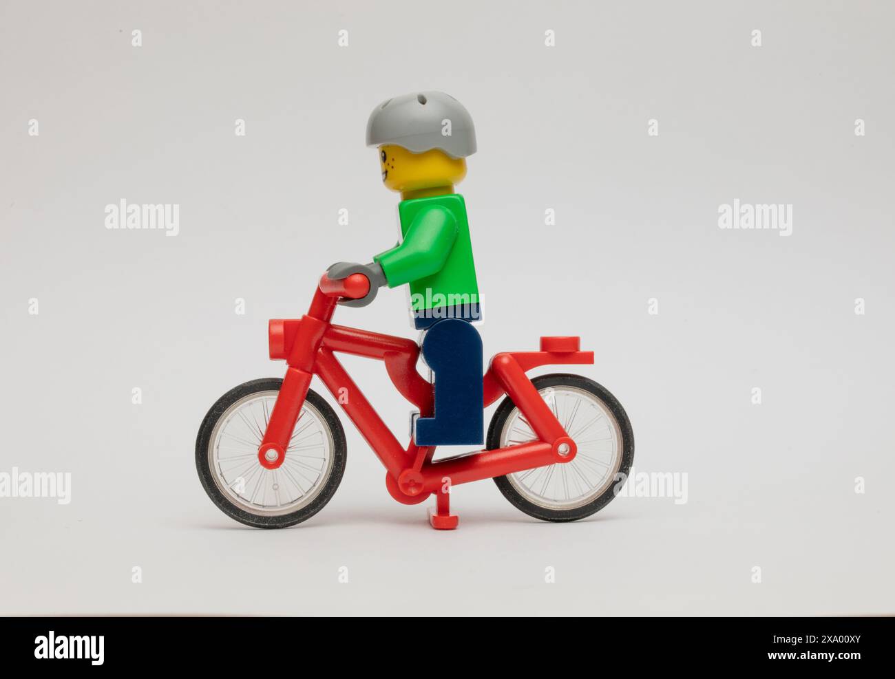 A Lego minifigure of a boy with a safety helmet riding a red bicycle ...