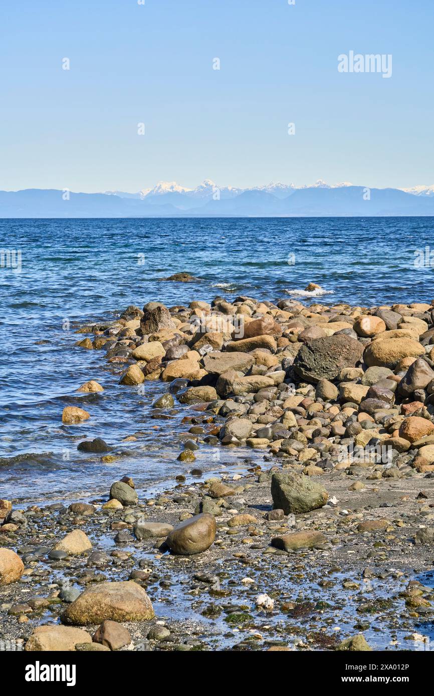 A rocky reef reaching out into the blue ocean with distant snow capped ...