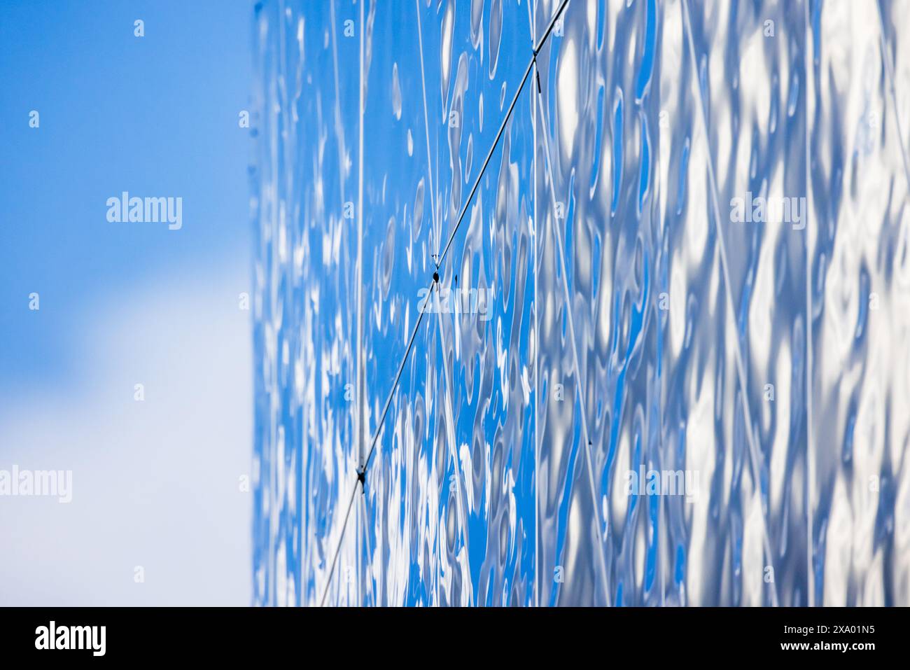Shiny blue metal wall made of rippled steel plates reflects cloudsy sky ...