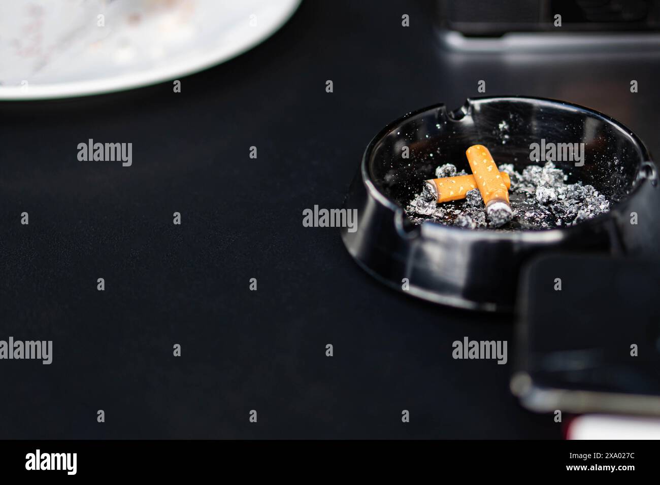 Close-up of a black ashtray with cigarette butts and ashes on a dark ...