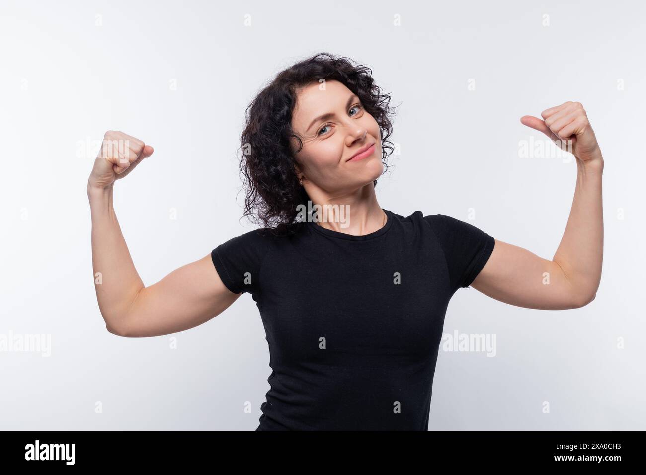 Caucasian woman with black curls shows her strong muscles Stock Photo ...
