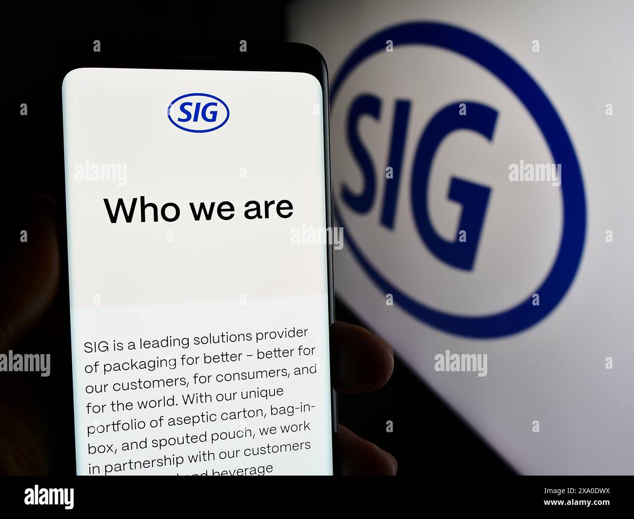 Person holding smartphone with webpage of Swiss packaging company SIG Group AG in front of ...