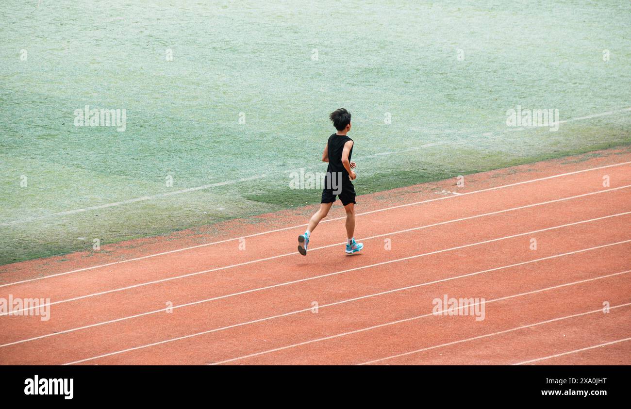 A young student doing long-distance running on a red university track ...