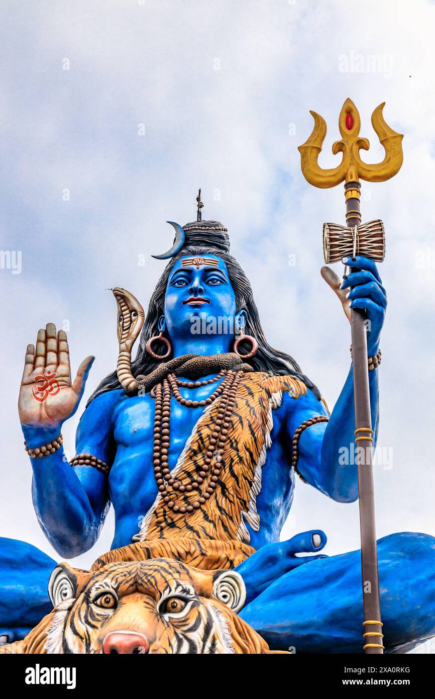 Blue statue of Lord Shiva seated with a tiger skin, holding a trident ...