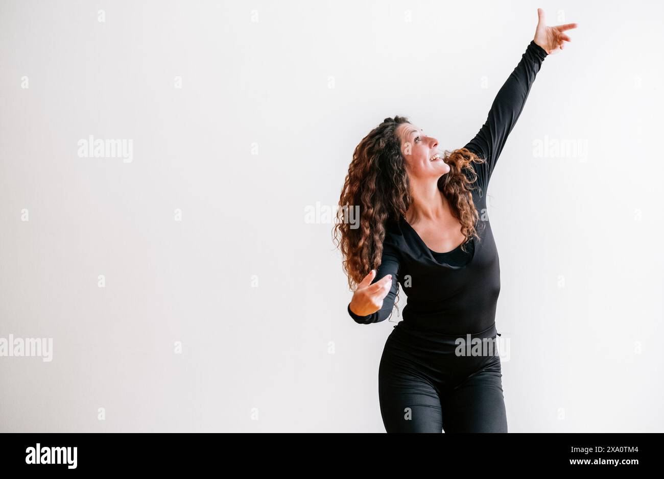 Joyful woman in black outfit captured mid-dance in bright room arms ...