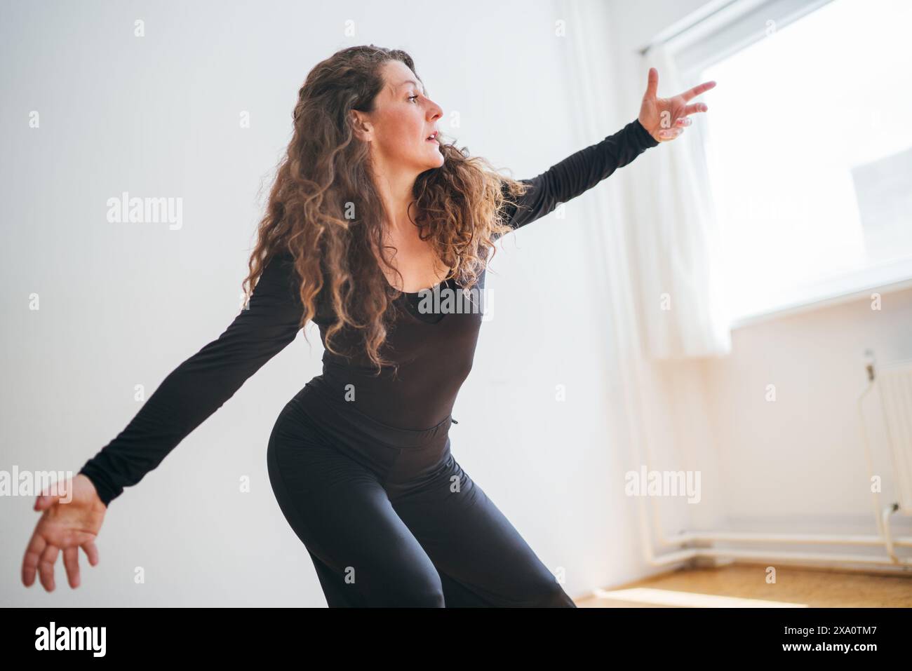 Woman in a black outfit gracefully dances in a well-lit room, her ...