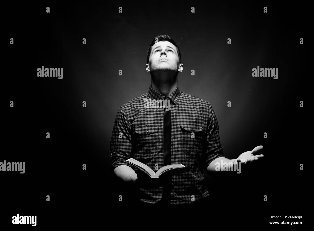 A black and white image of a man looking up with a book in one hand and ...