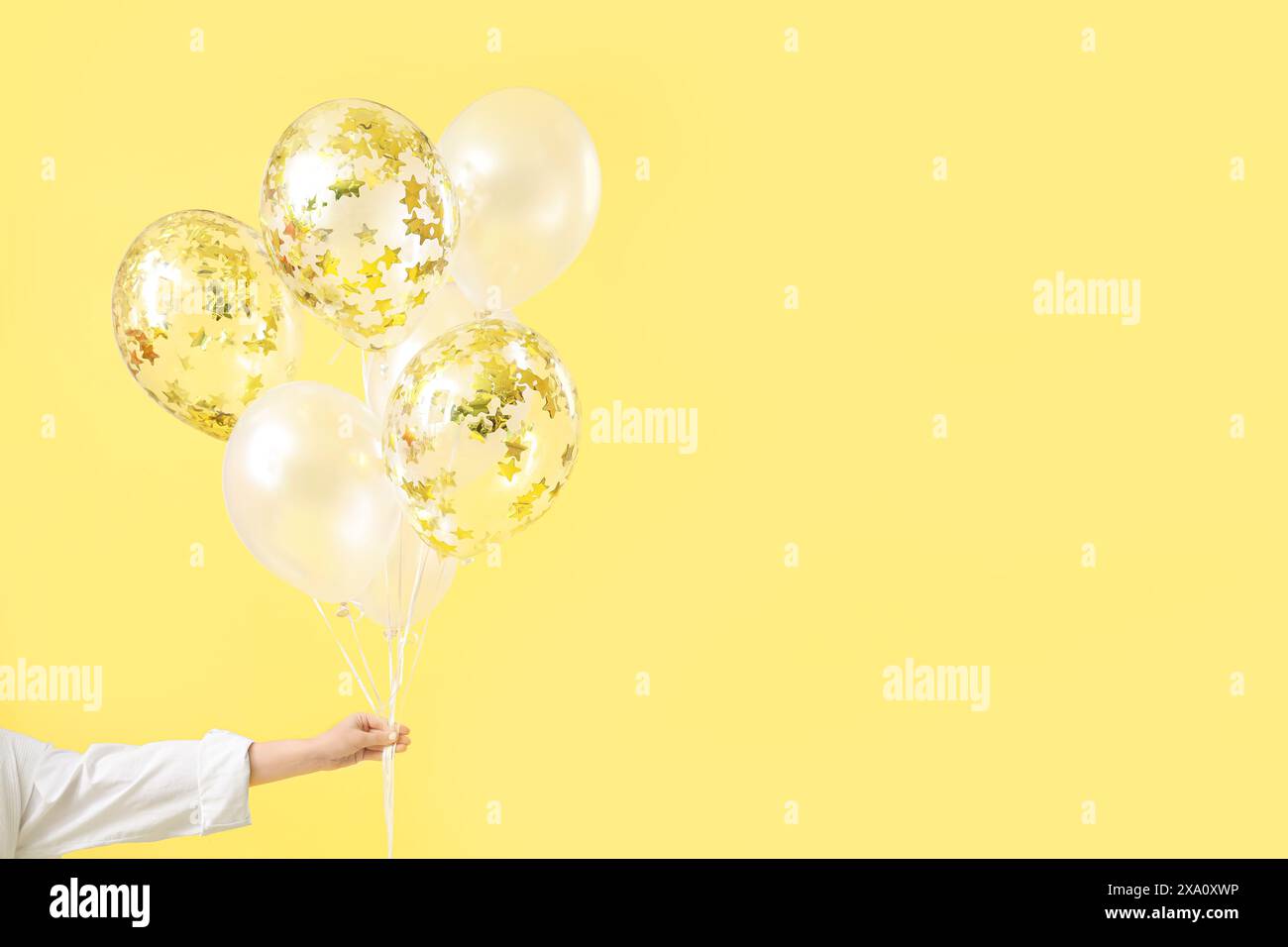 Female hand holding floating balloons on yellow background Stock Photo ...