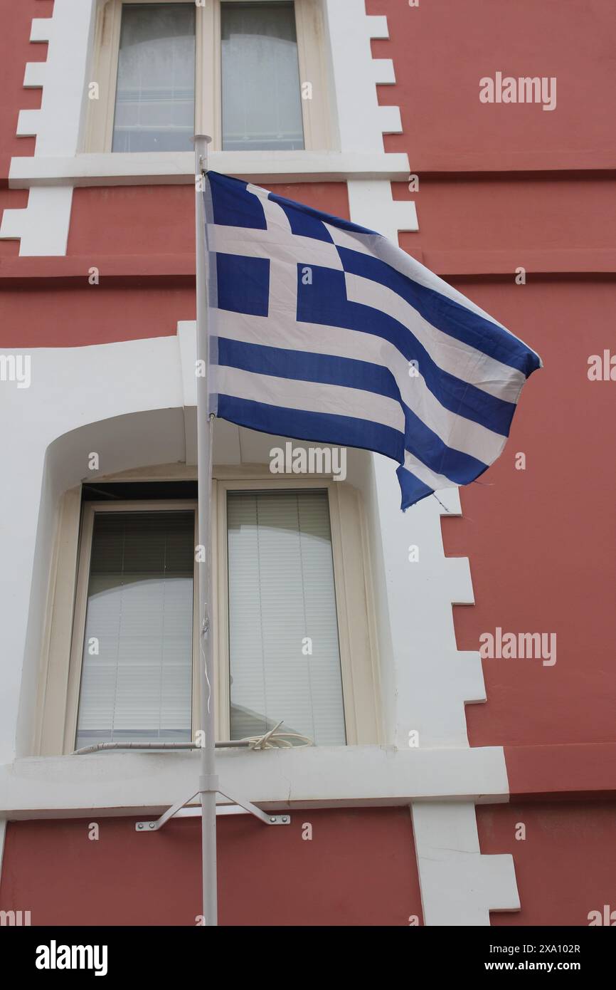 The Greek flag waving in front of red building Stock Photo - Alamy