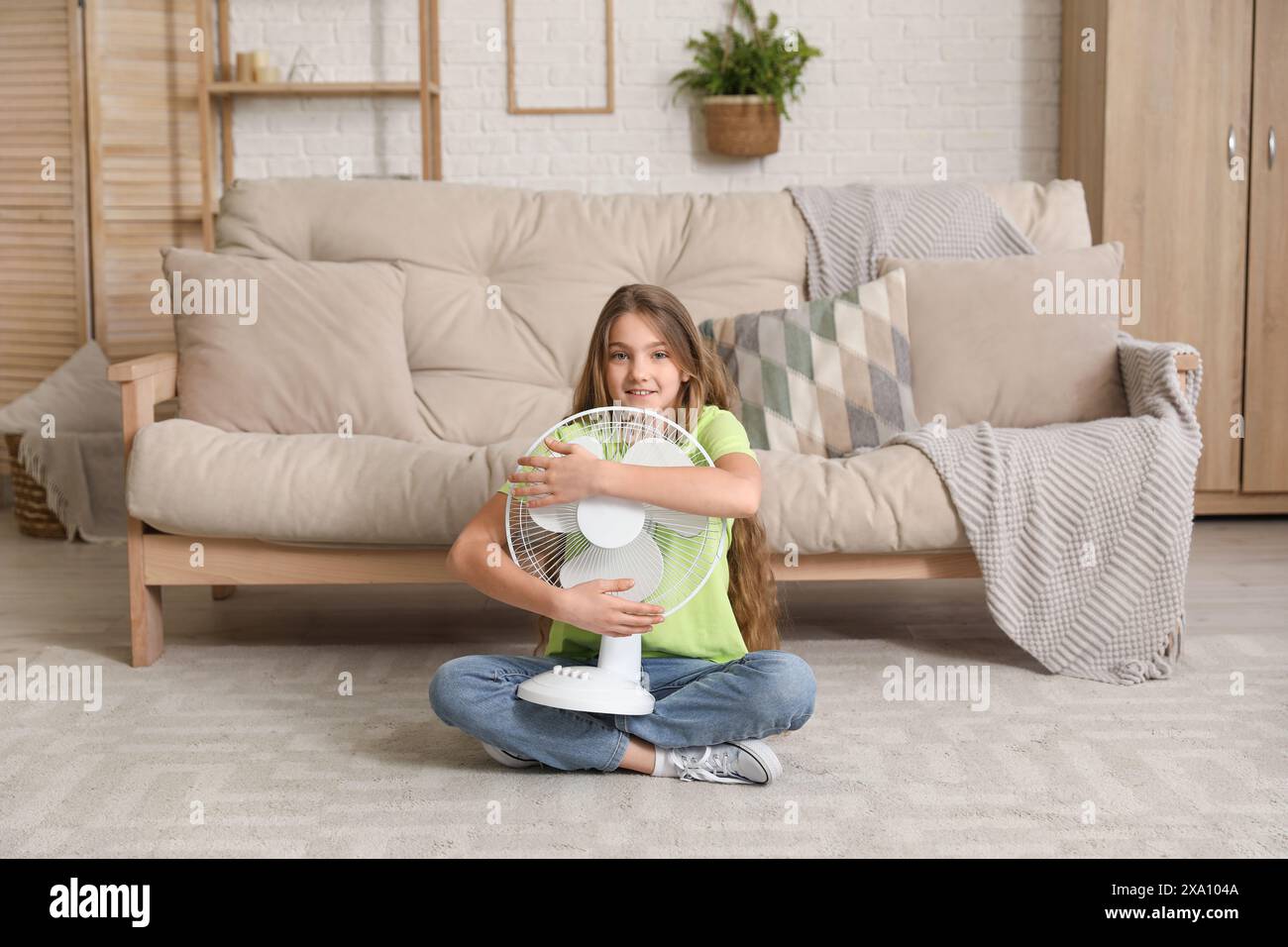 Teenage girl sitting on floor and hugging electric fan in living room ...