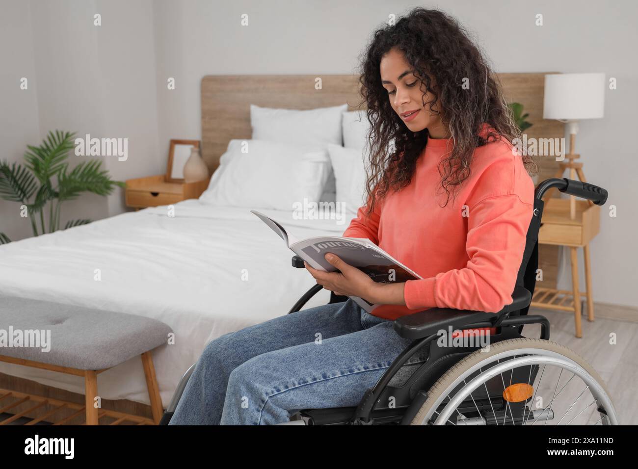 Young African-American woman in wheelchair reading magazine at home ...