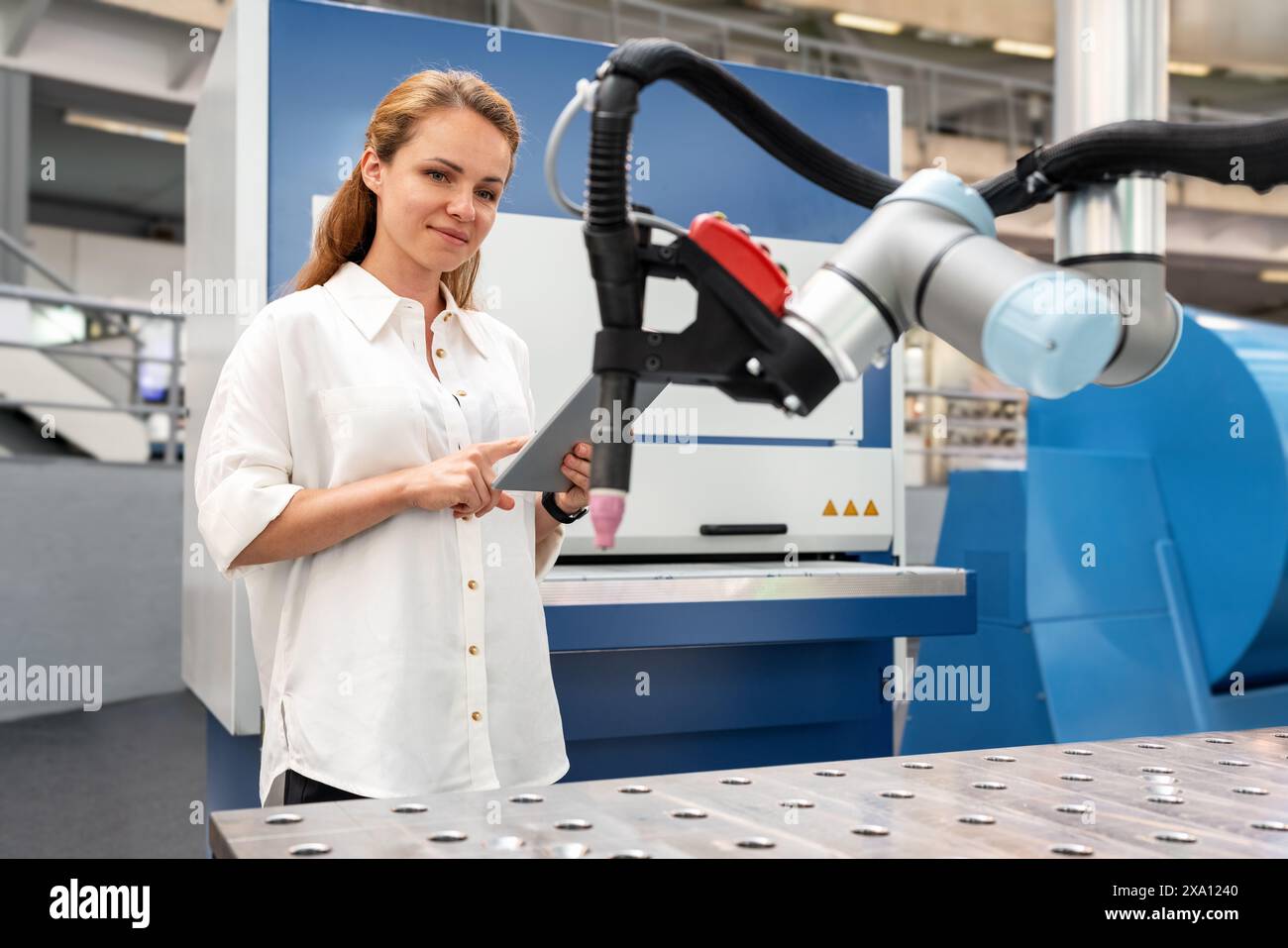 Young adult female entrepreneur controls robotic arm in startup factory using wireless ...