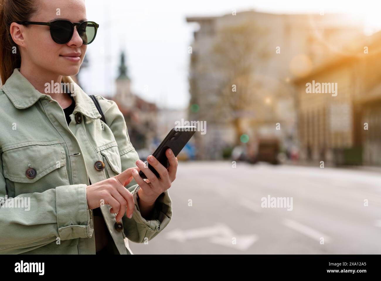 Female urban person stands near the city road and booking a taxi using ...