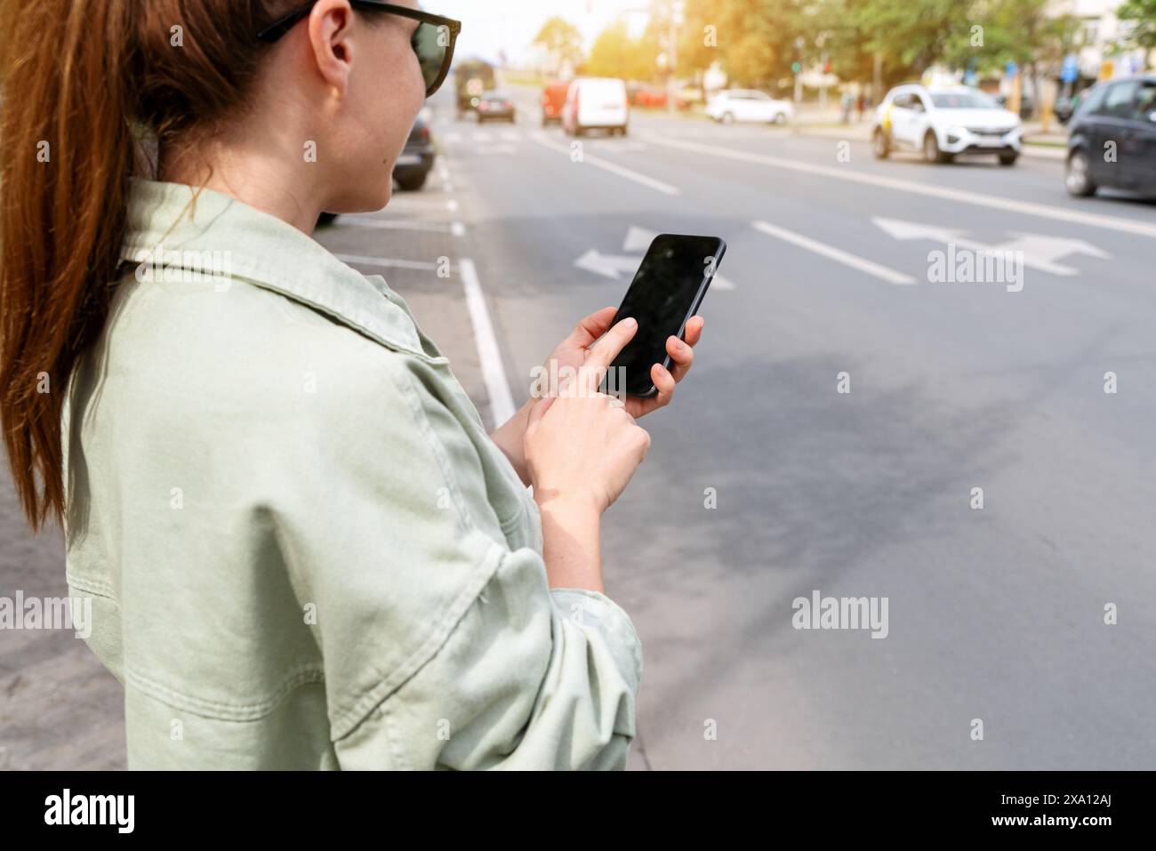 Female urban person stands near the city road and booking a taxi using ...