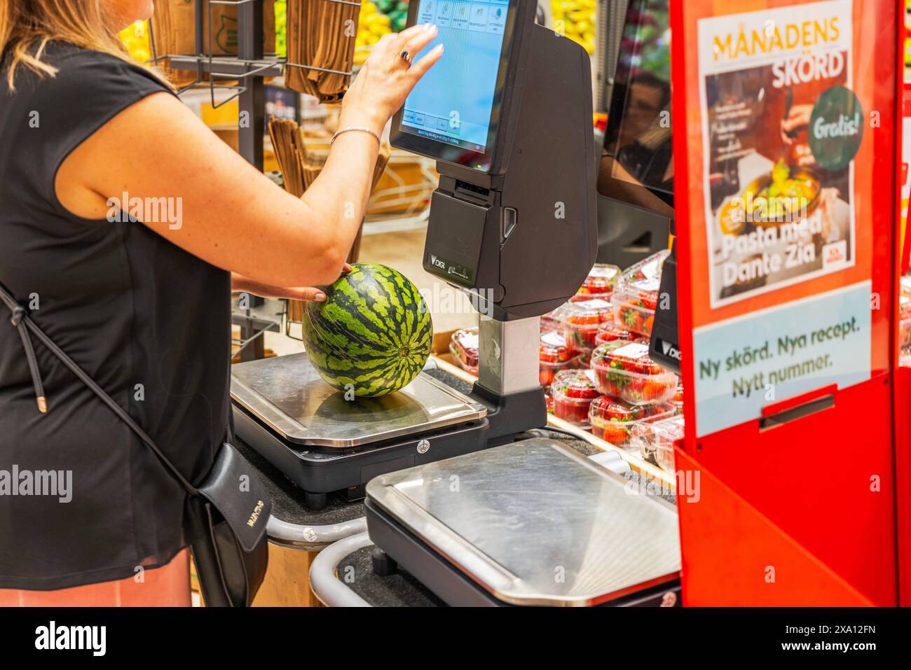 Close-up view of a woman weighing a watermelon at a self-checkout kiosk ...