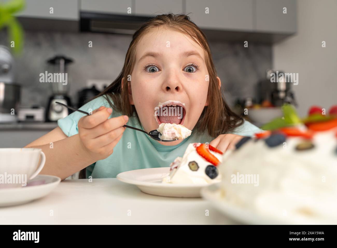 Crazy little girl eating cake with a big spoon. A pre-teenage girl eats ...